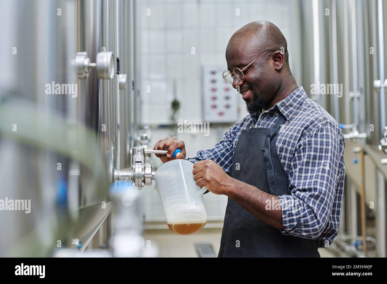African American factory worker pouring brewed beer in container for ...