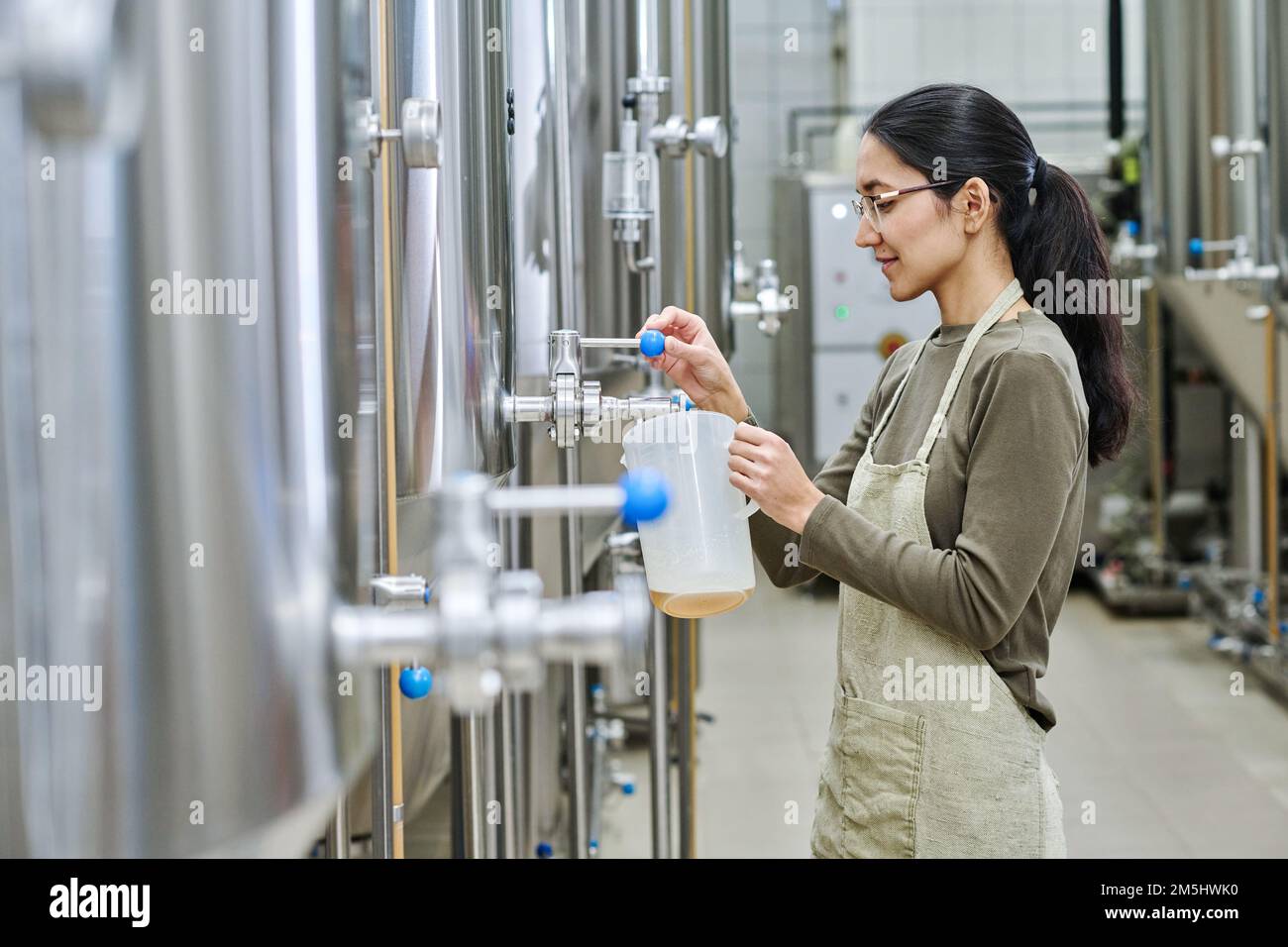 Worker pouring brewed beer in container for degustation during her work ...