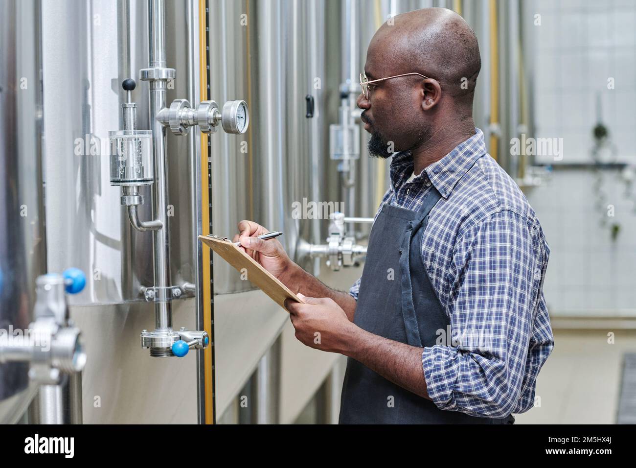 African American worker writing indicators of gauge in document while ...