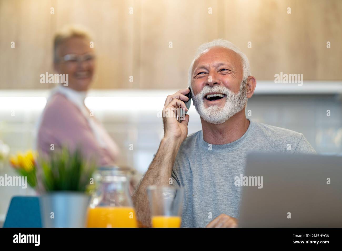 Senior man talking on phone and using laptop, he is working from home ...