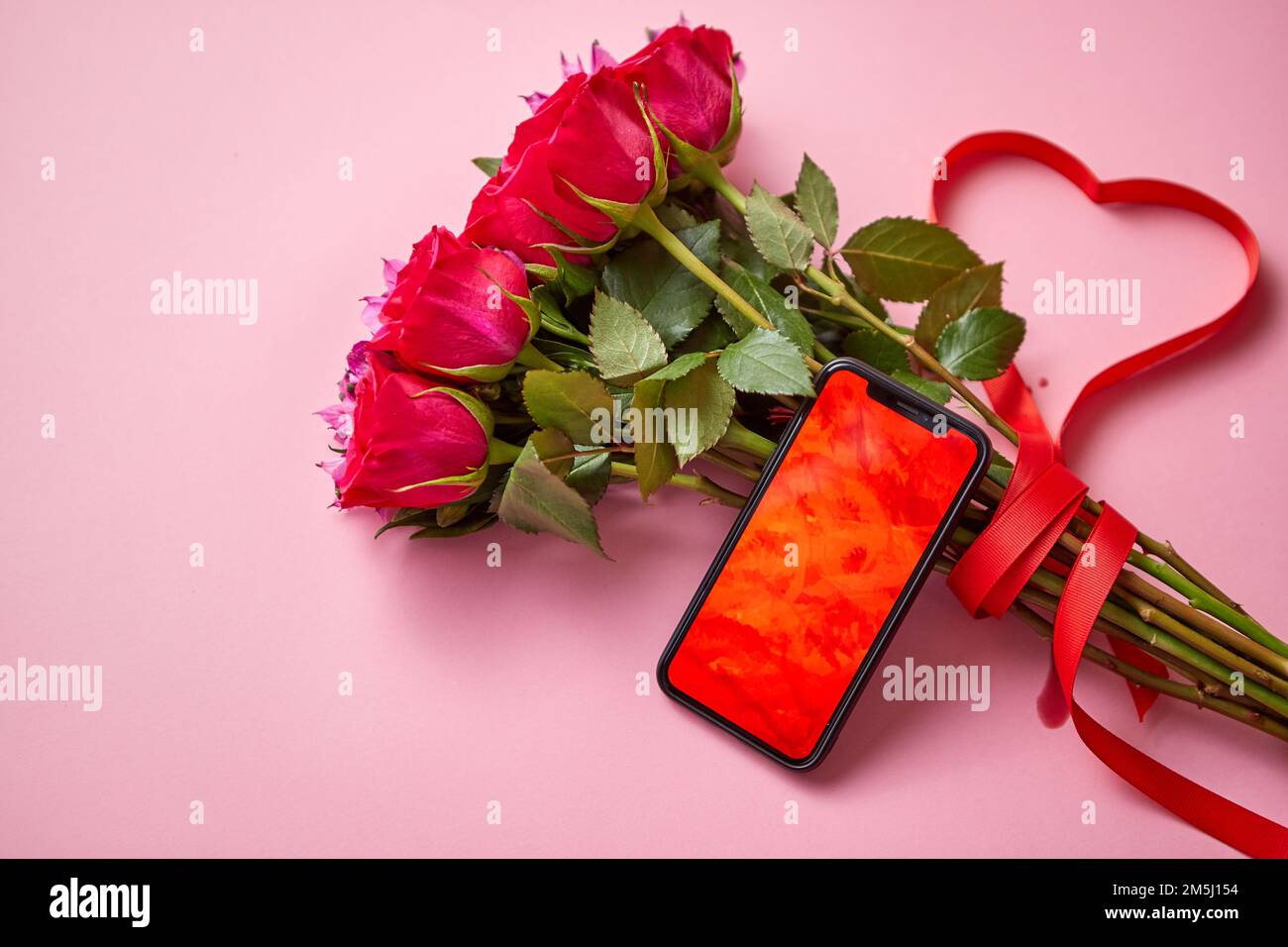 Pink roses bouquet with hart shaped bow and mobile phone with copy ...