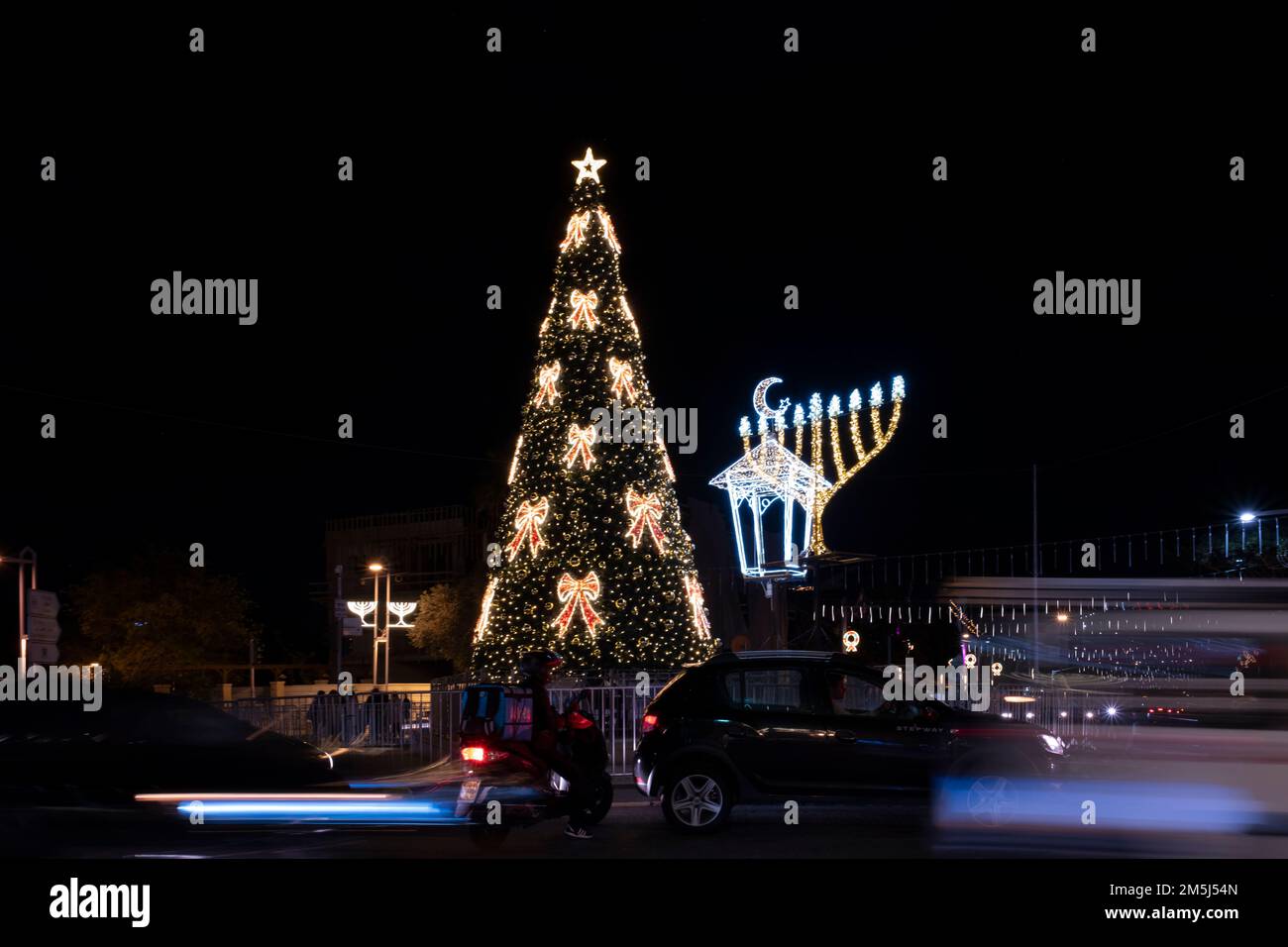Cars pass by a decorated Christmas tree with illuminated Hanukkah ...