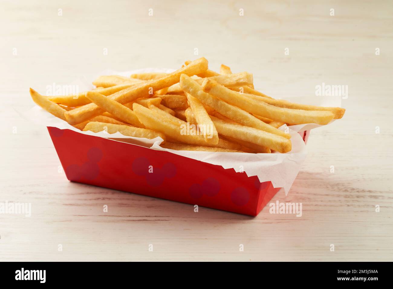 One serving of French fries in a cardboard container on wooden table ...