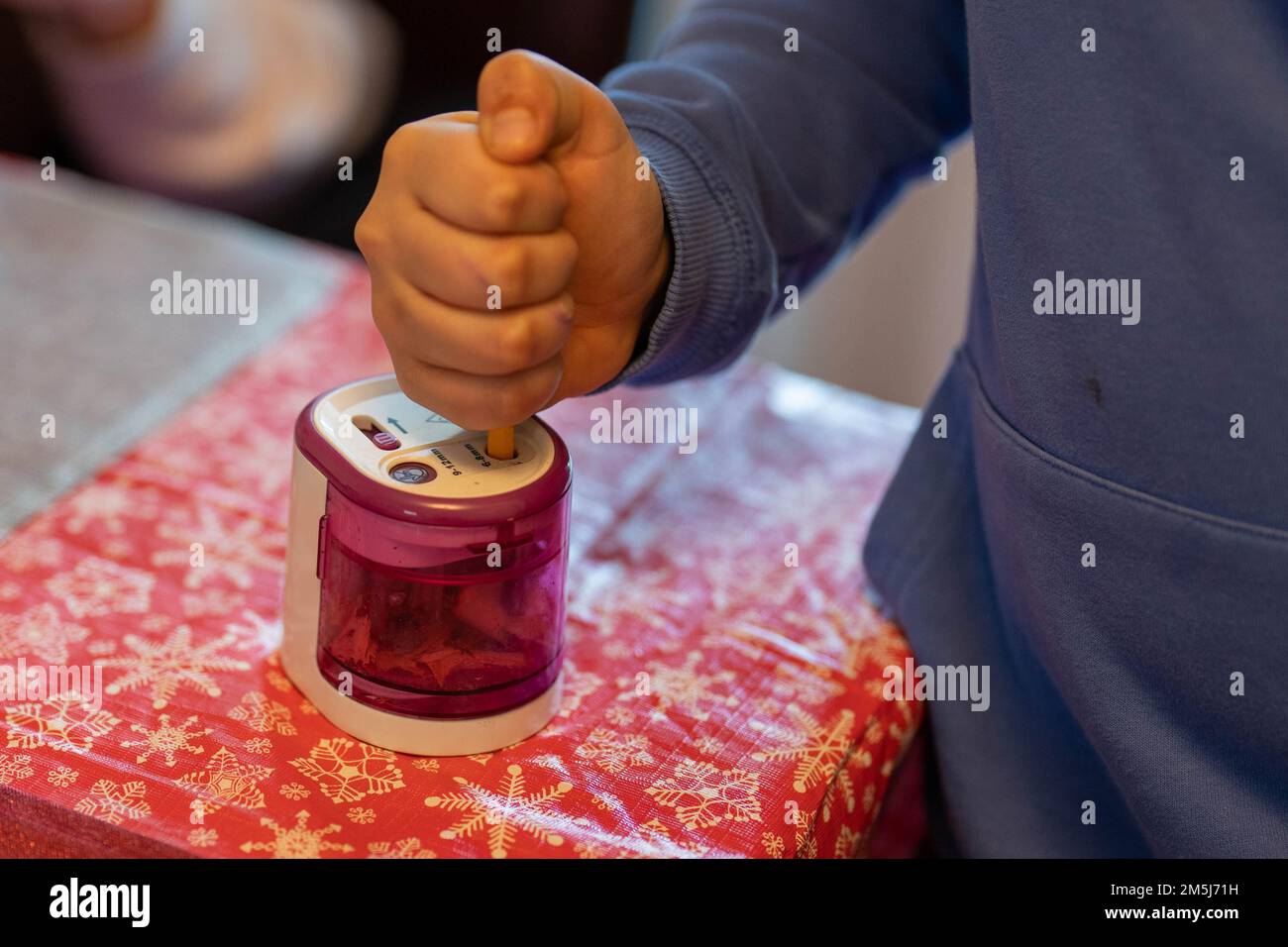 Child sharpening a pencil with a battery operated pencil sharpener on a ...