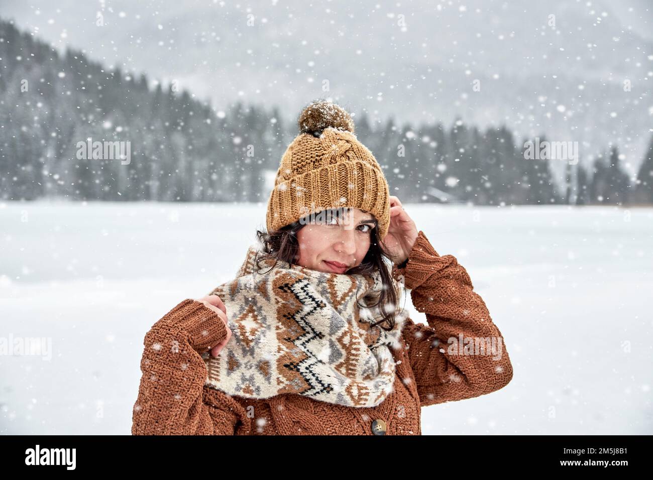 A woman in a cozy winter sweater and scarf looking at the camera under ...