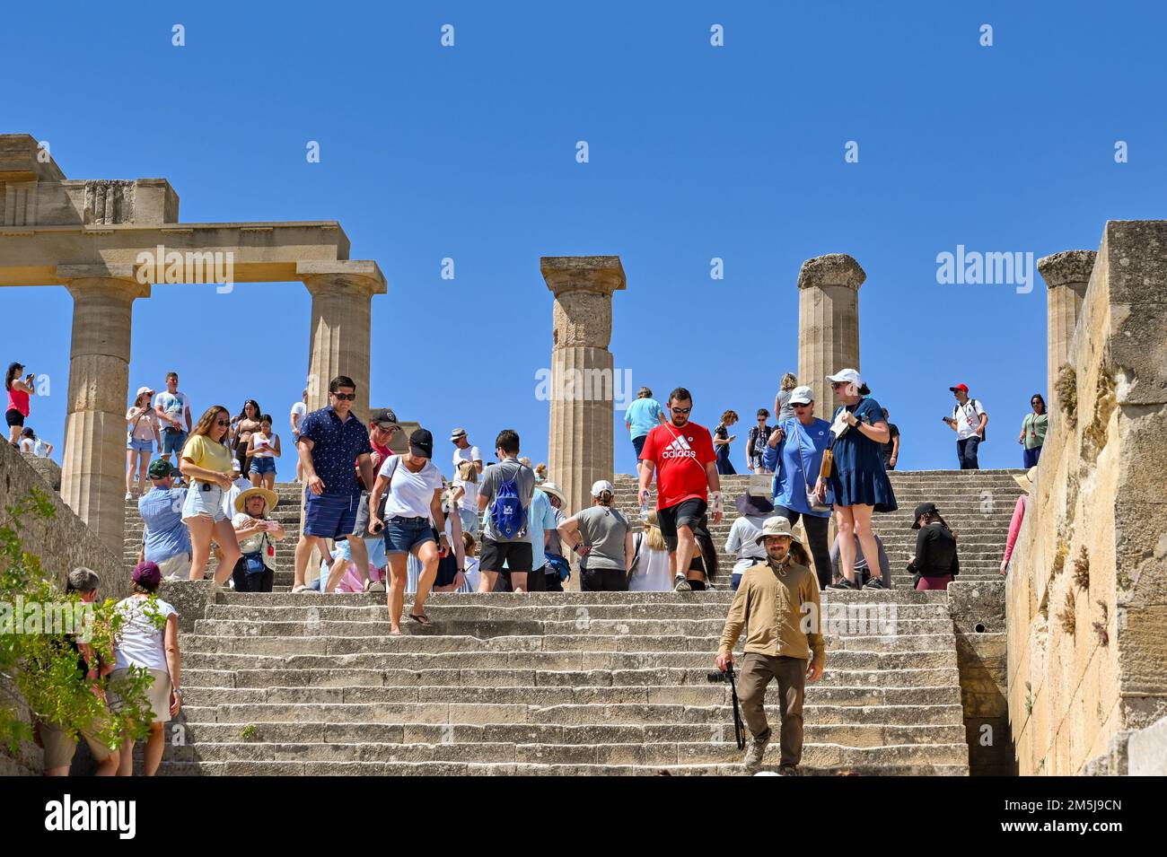 Lindos, Rhodes, Greece - May 2022: Tourists visiting the ancient ruins of the acropolis above ...