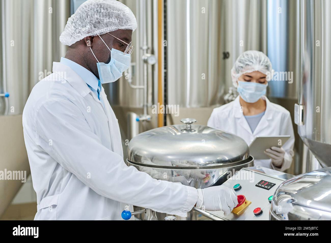 Engineer in protective clothing pushing button on equipment while ...