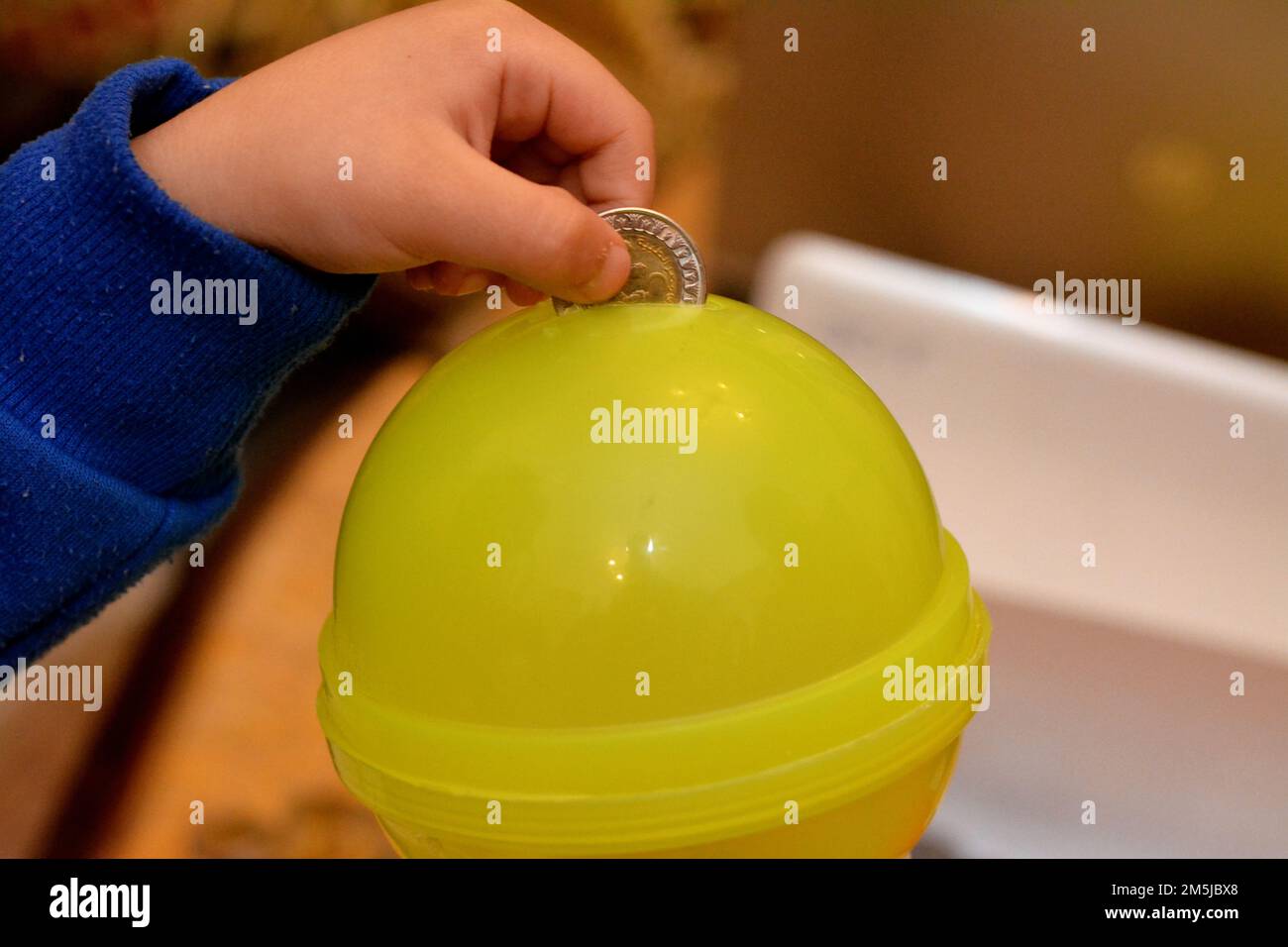 A young child putting a coin in a plastic child saving bank, concept of ...