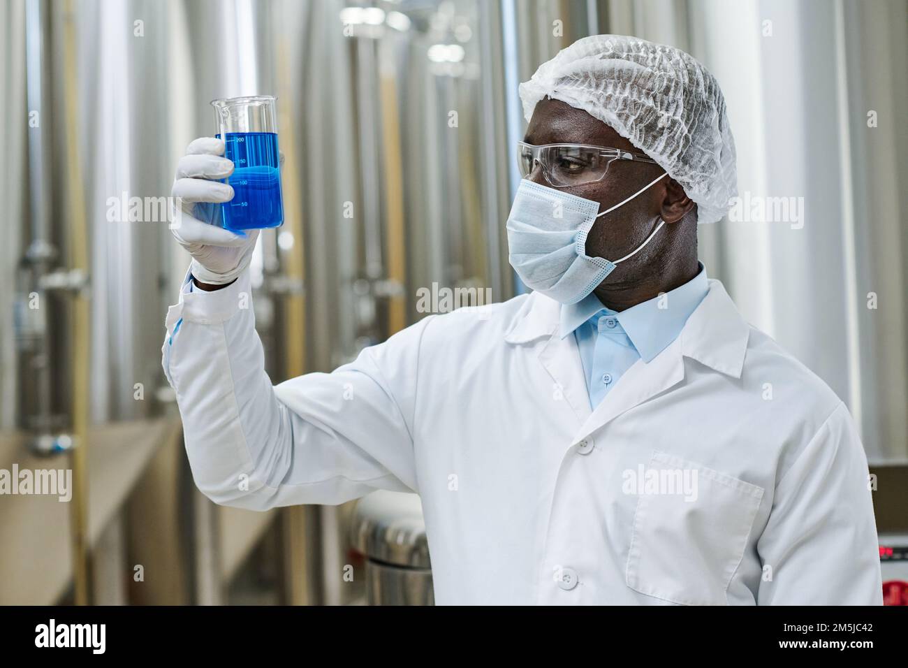 African American engineer in protective mask and lab coat examining ...