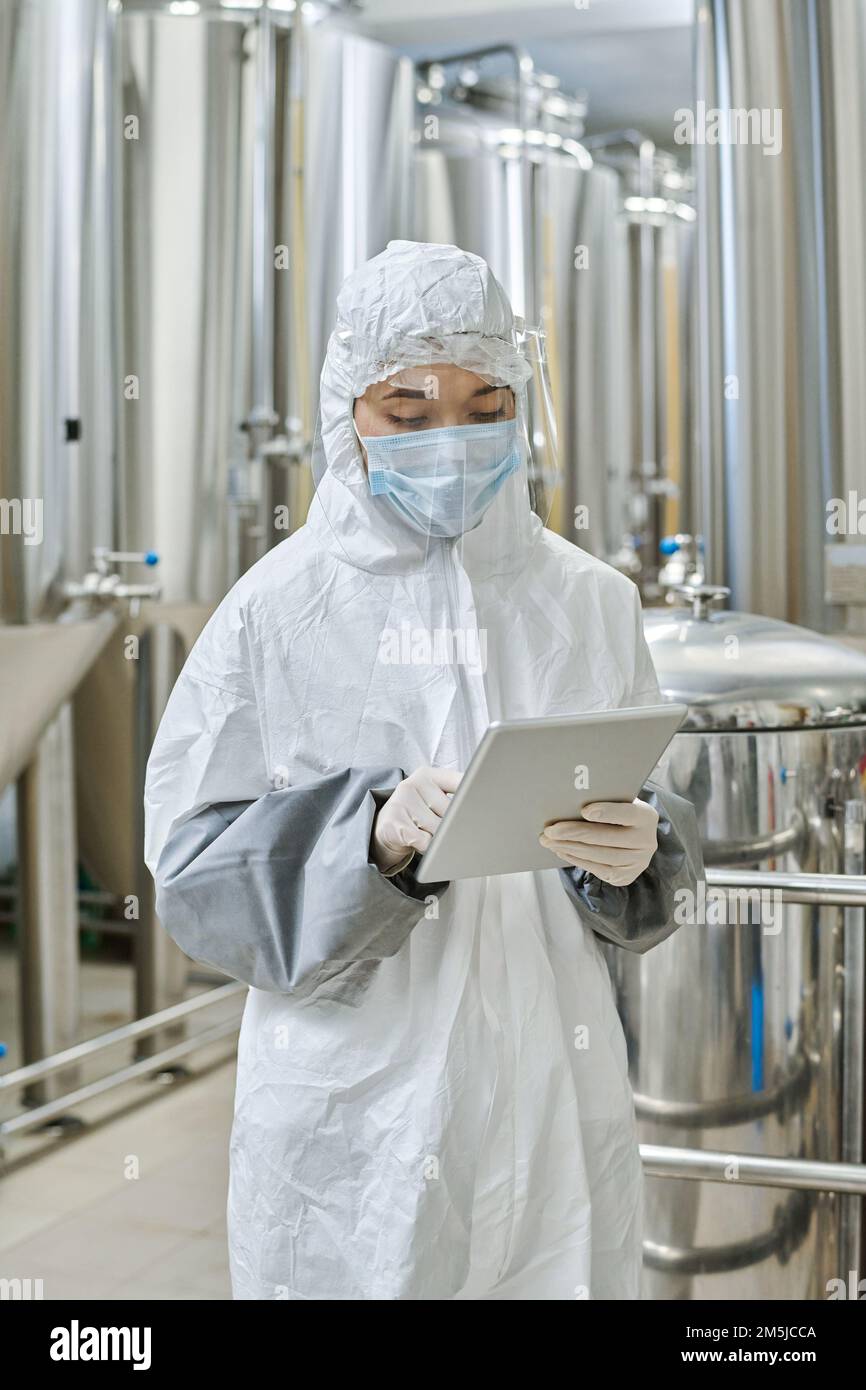 Young engineer in protective wear and mask working on tablet pc ...