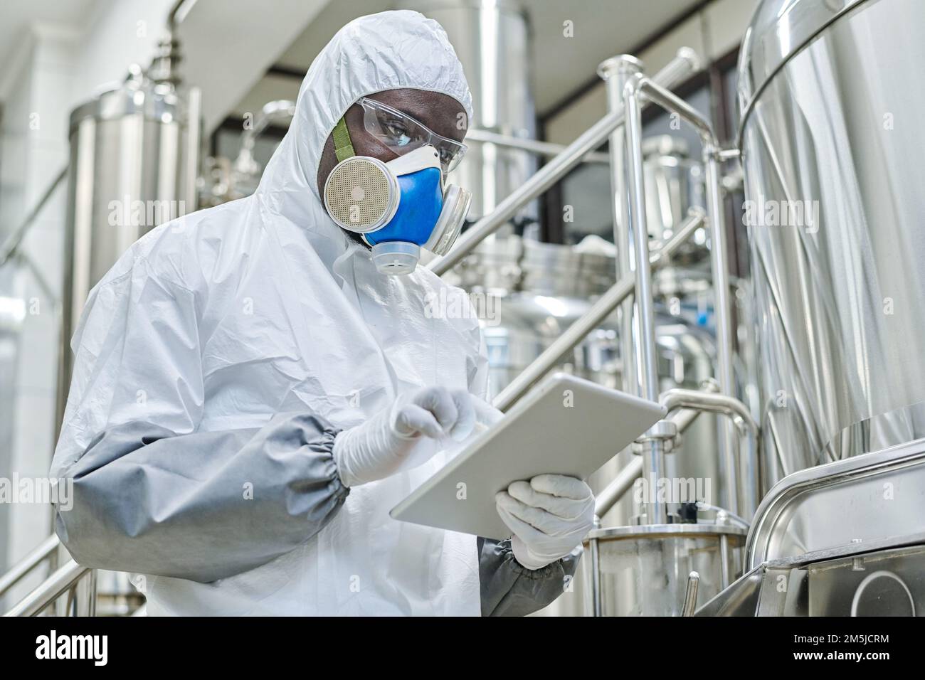 African American chemist in protective costume working online on tablet ...