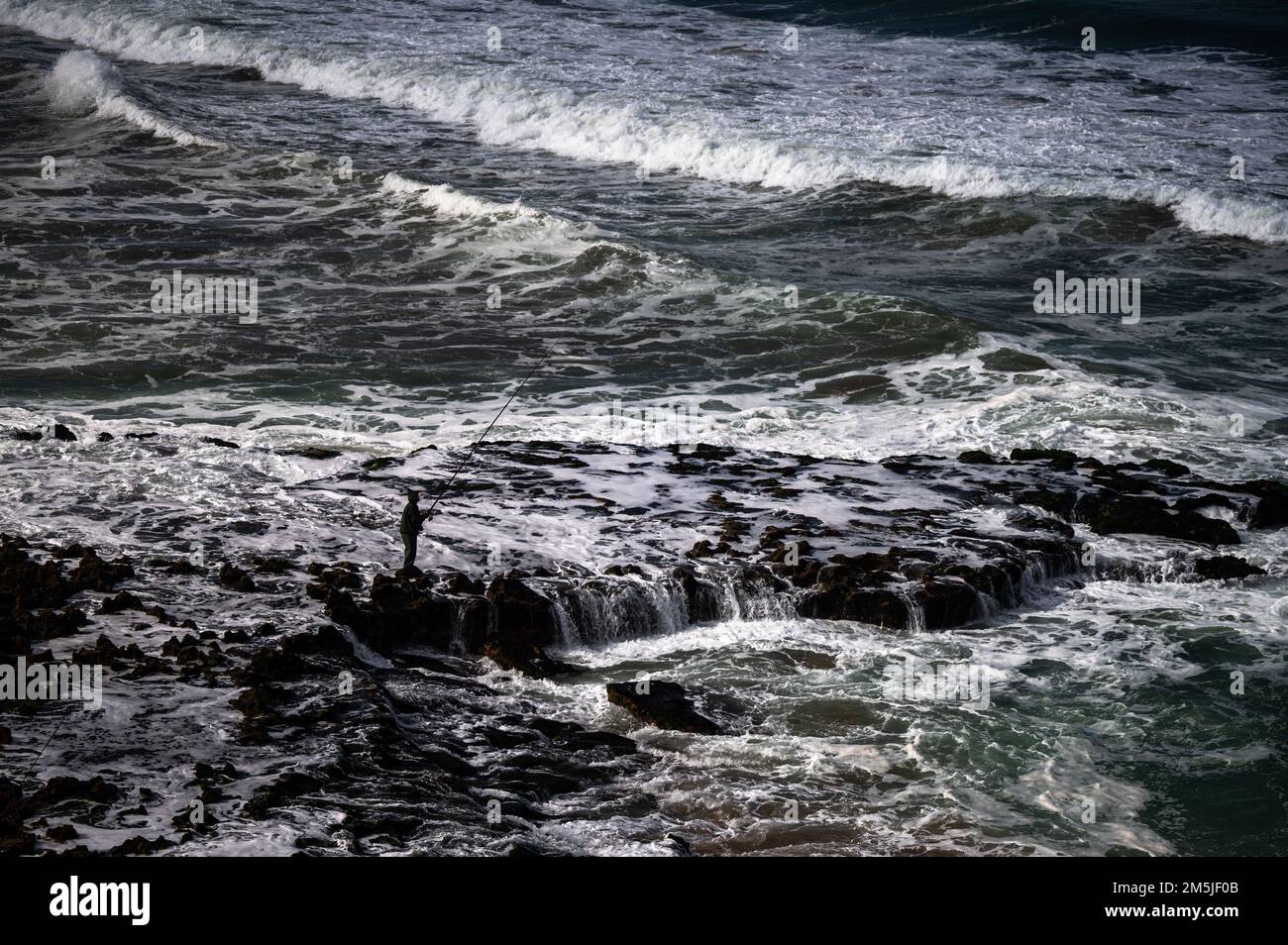 Silhouette of a man fishing in the Atlantic Ocean during high tide ...