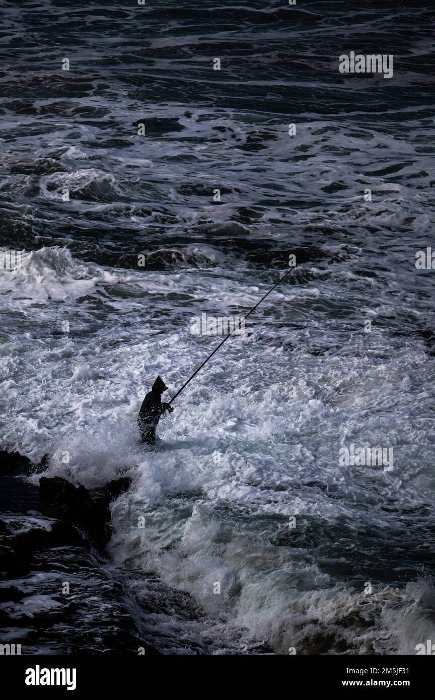 Silhouette of a man fishing in the Atlantic Ocean during high tide ...