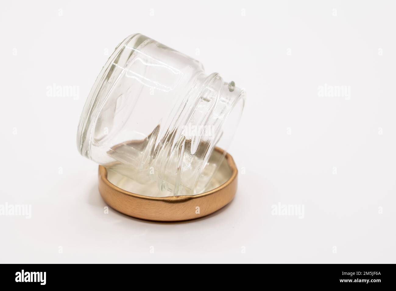 Close-up of a small empty clear jam preserve glass jar with a a bronze ...