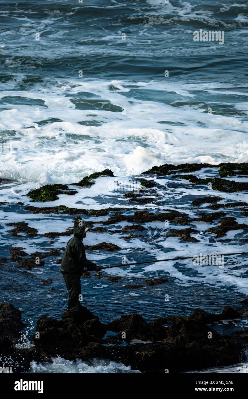Silhouette of a man fishing in the Atlantic Ocean during high tide ...
