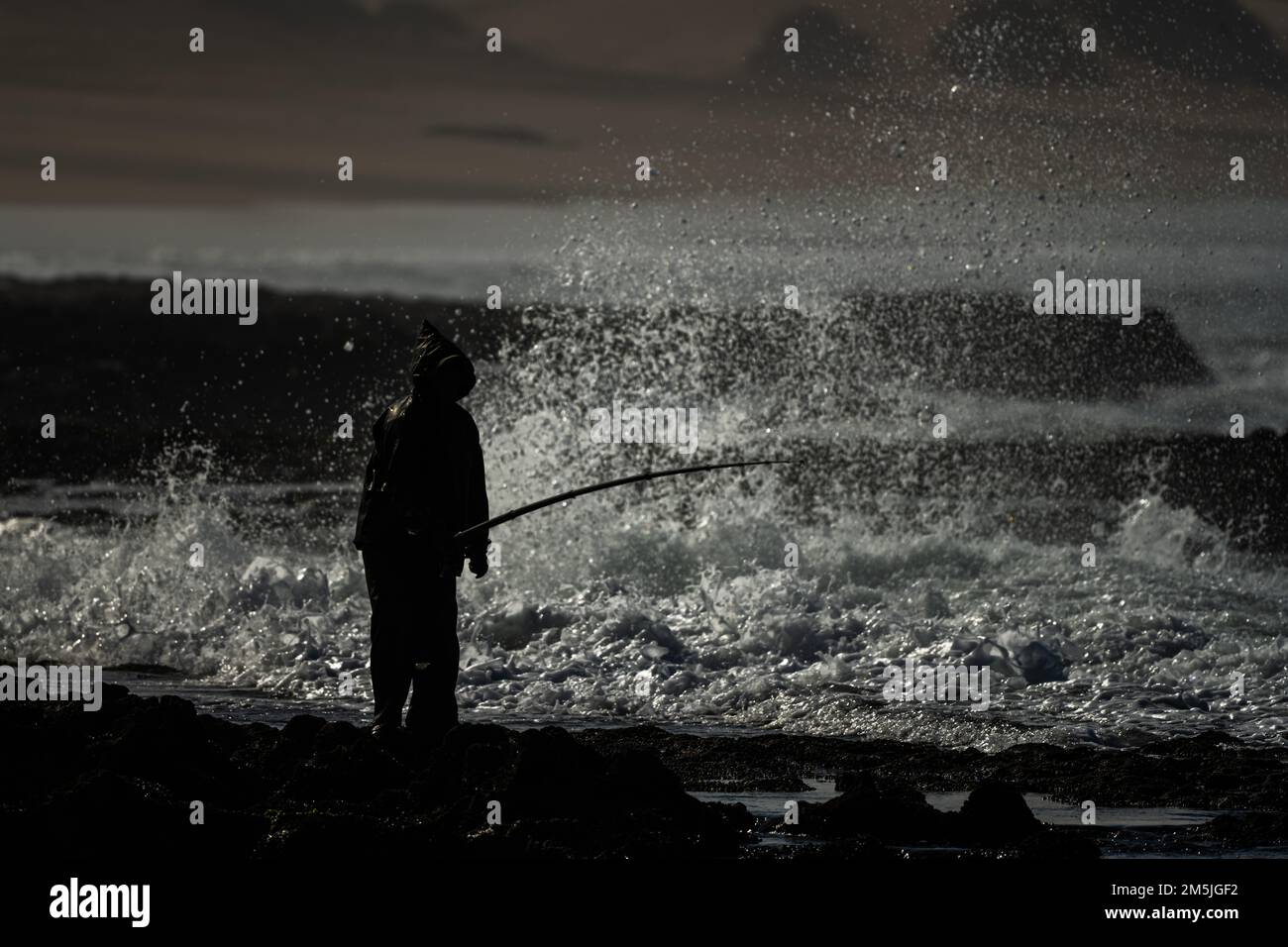 Silhouette of a man fishing in the Atlantic Ocean during high tide ...