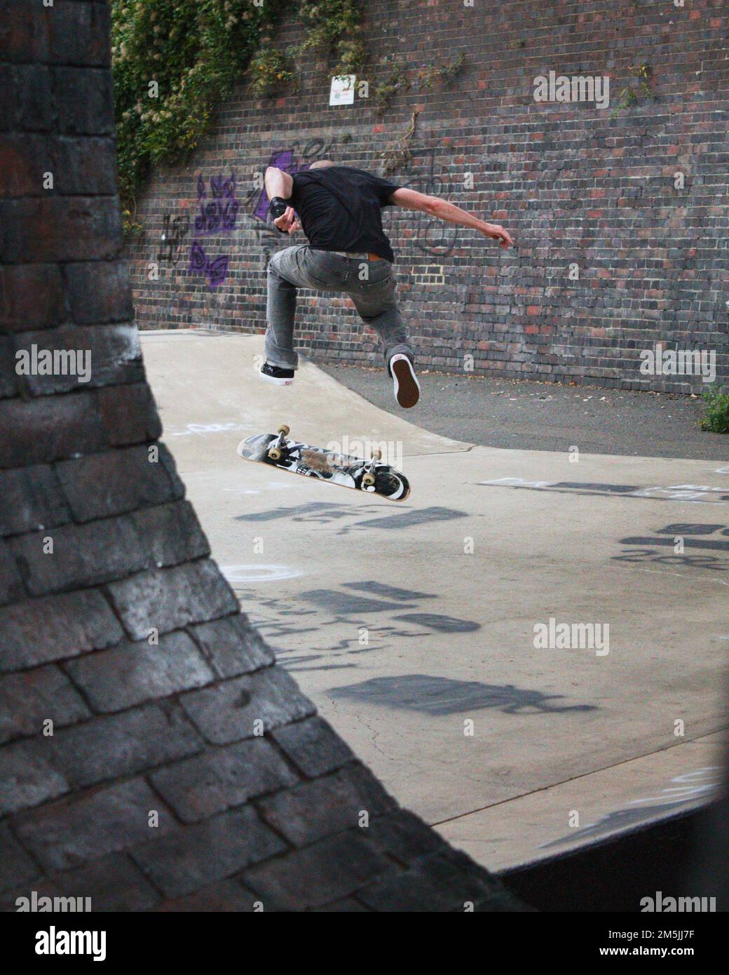 A vertical back view of a male skateboarder making tricks in a park ...
