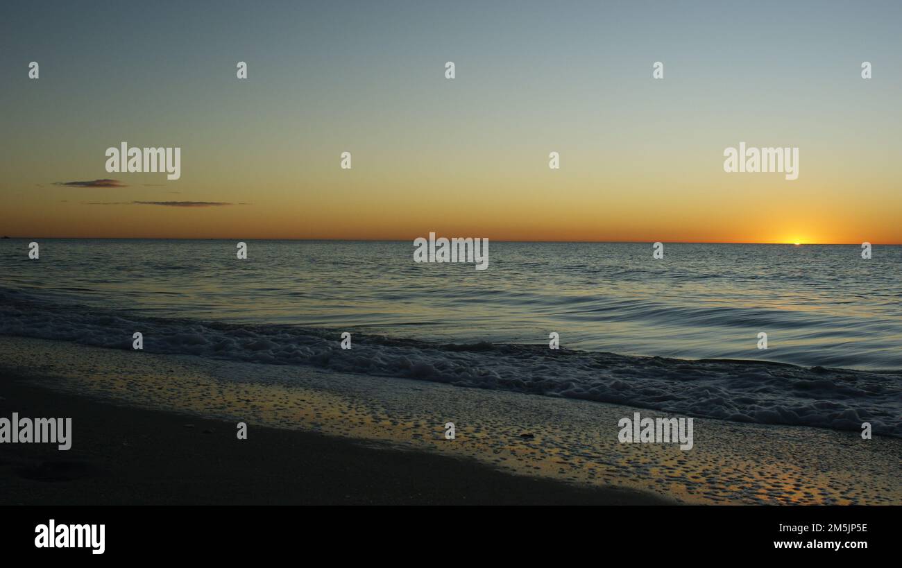 A sandy beach by gray dunes sea and golden sunset sky on the horizon ...