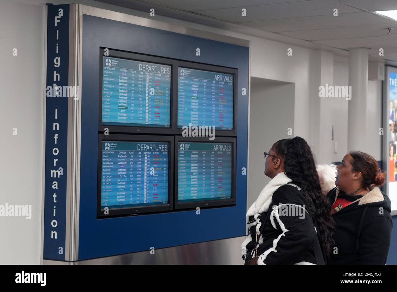 Passengers look at an rrivals and departures flight monitor with on ...