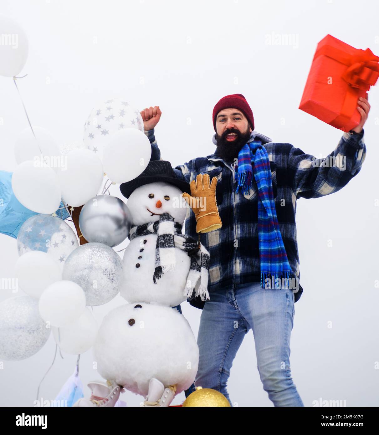 Bearded man in warm clothes with gift box. Snowman in hat, scarf and ...