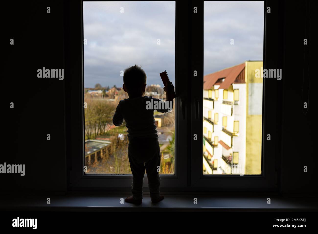 Lonely child standing on the windowsill. Dangerous situation, risk of ...