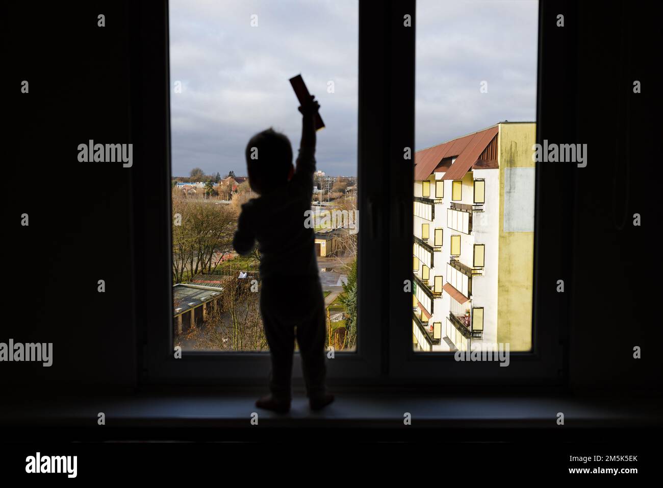 Lonely child standing on the windowsill. Dangerous situation, risk of ...