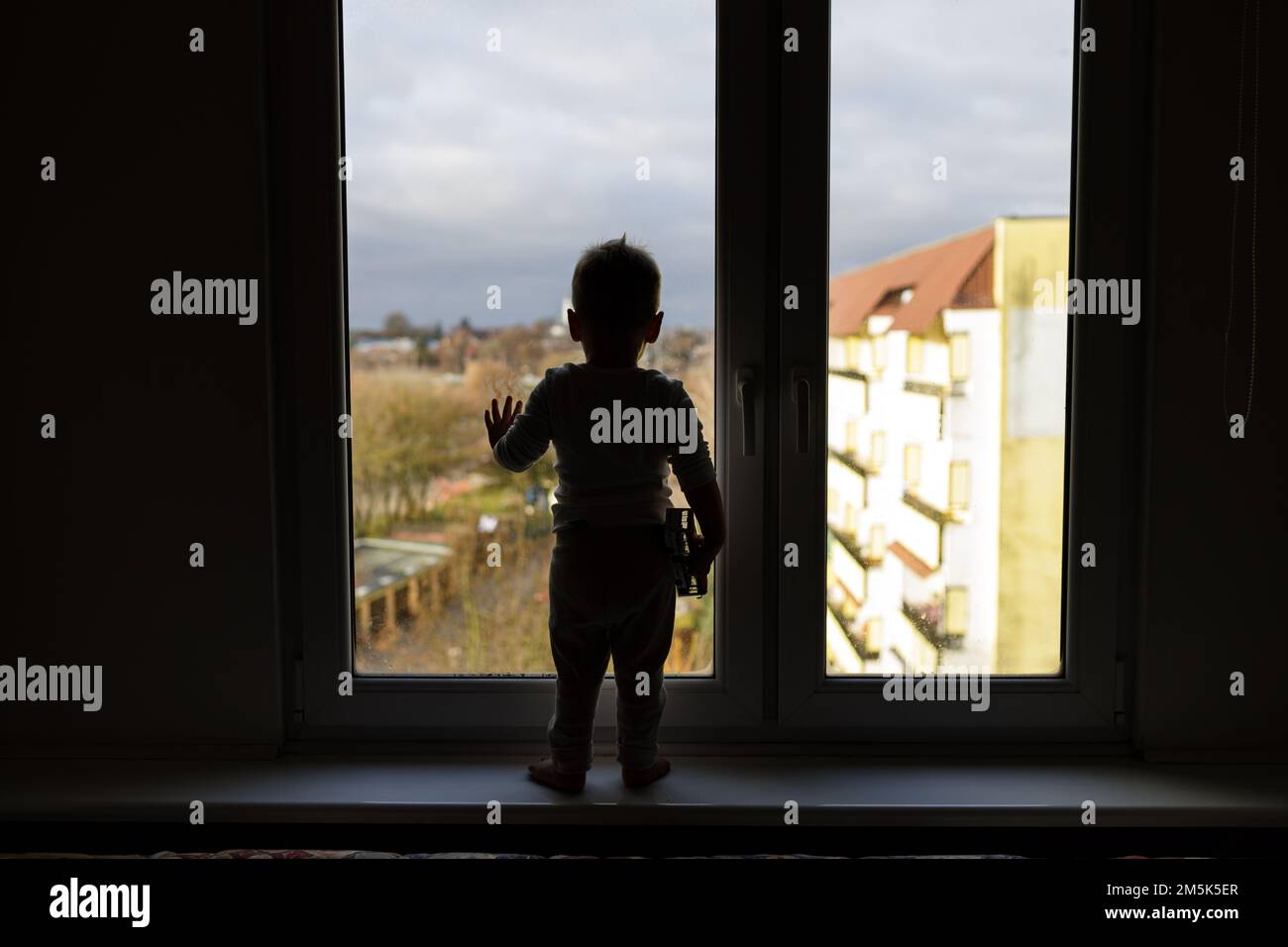 Lonely child standing on the windowsill. Dangerous situation, risk of ...