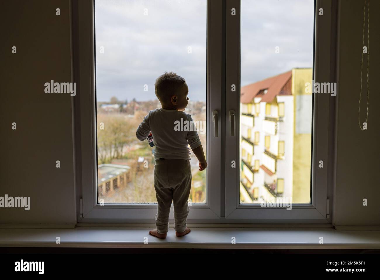 Lonely child standing on the windowsill. Dangerous situation, risk of ...