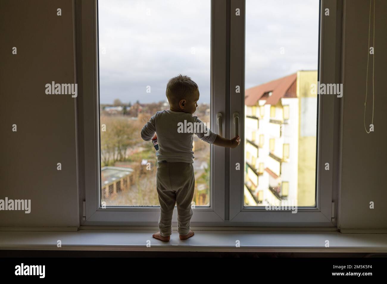 Lonely child standing on the windowsill. Dangerous situation, risk of ...