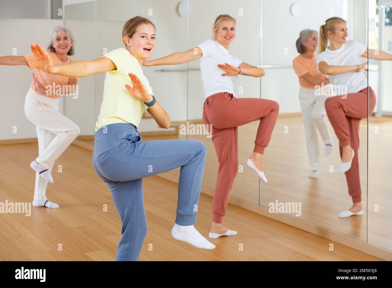 Teen girl with family exercising dance moves with group of people in ...