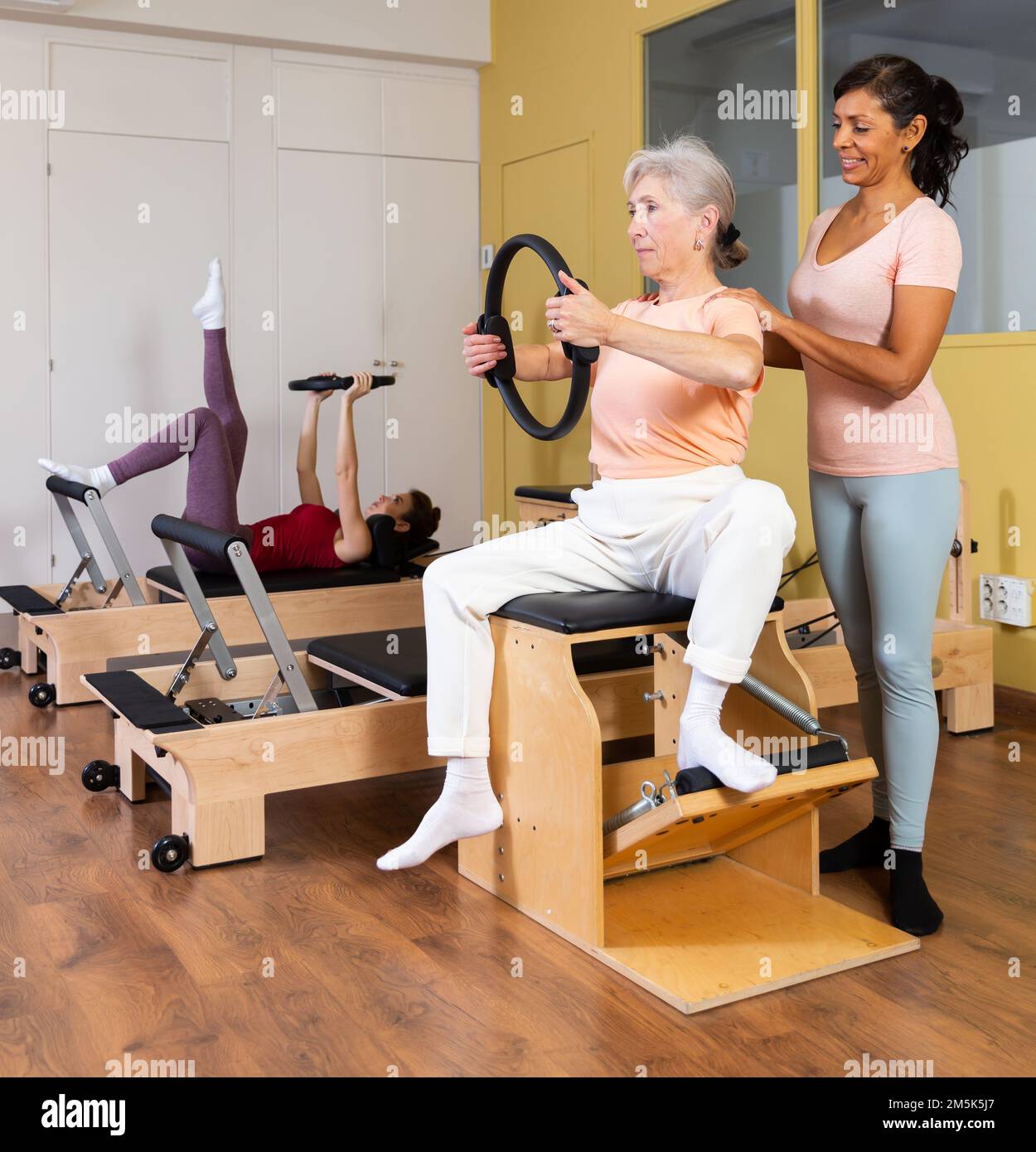 Elderly woman with trainer practicing pilates on combo chair with magic ...