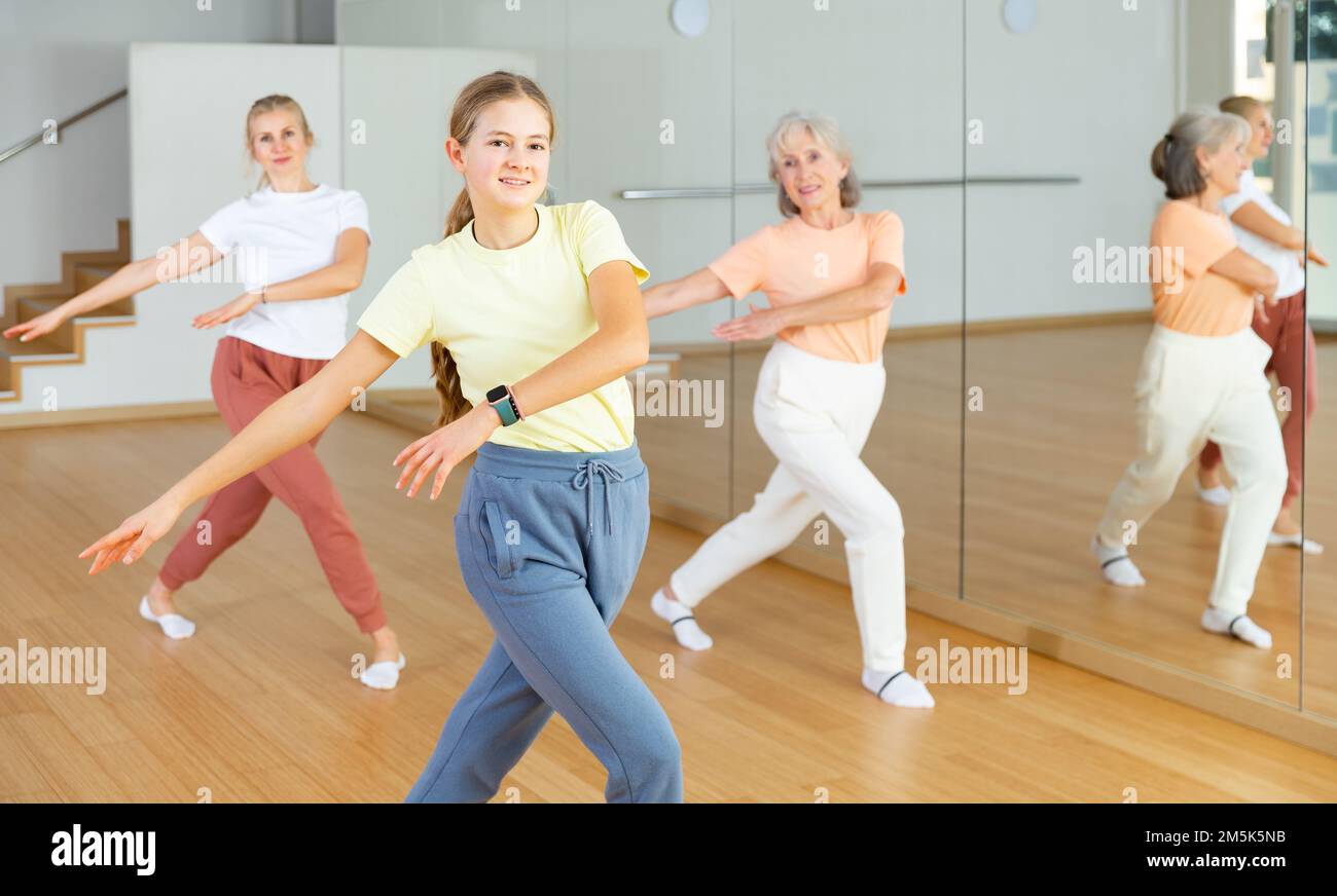 Teen girl with family exercising dance moves with group of people in ...