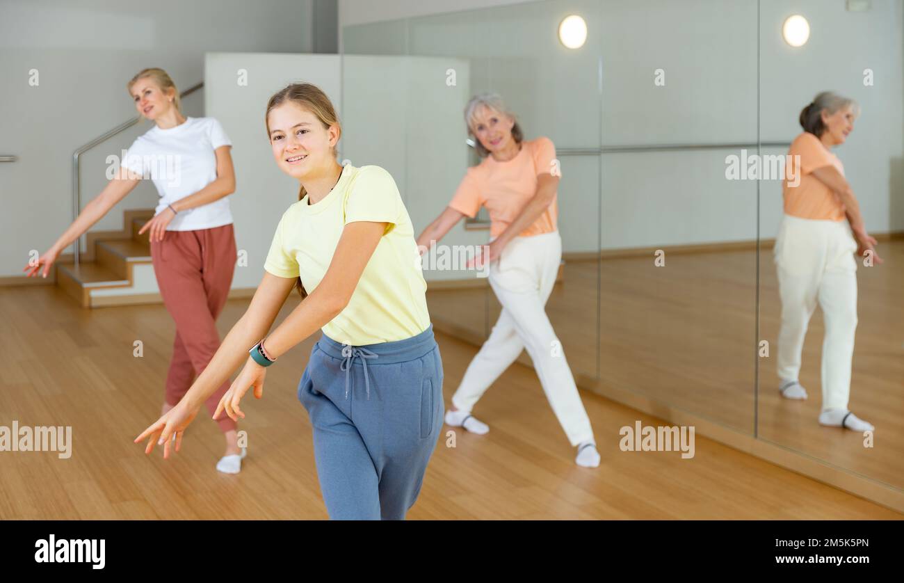 Teen girl with family exercising dance moves with group of people in ...