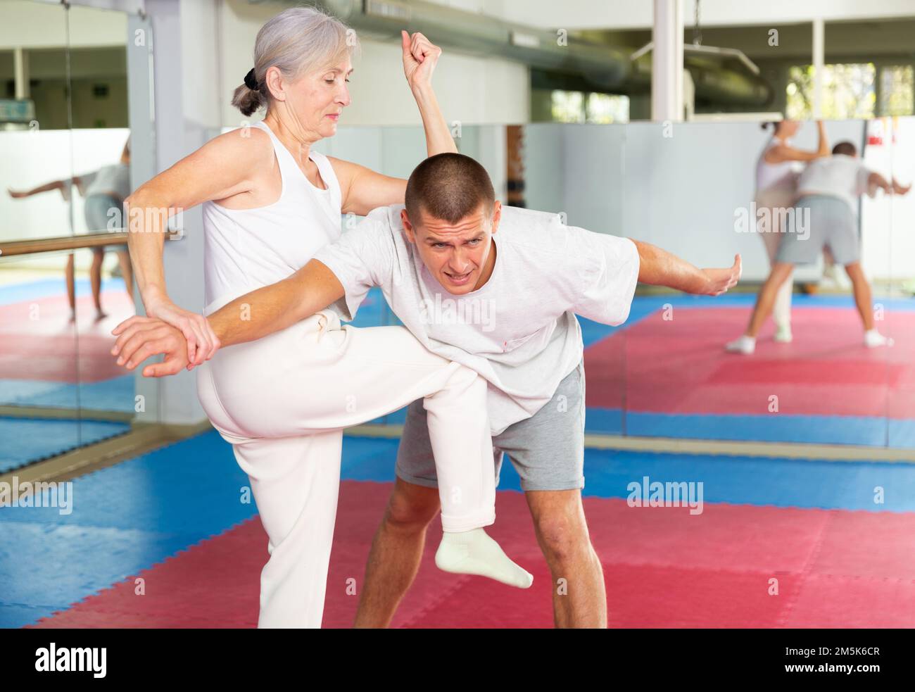 Elderly woman practicing elbow and knee strikes with arm hold to male ...