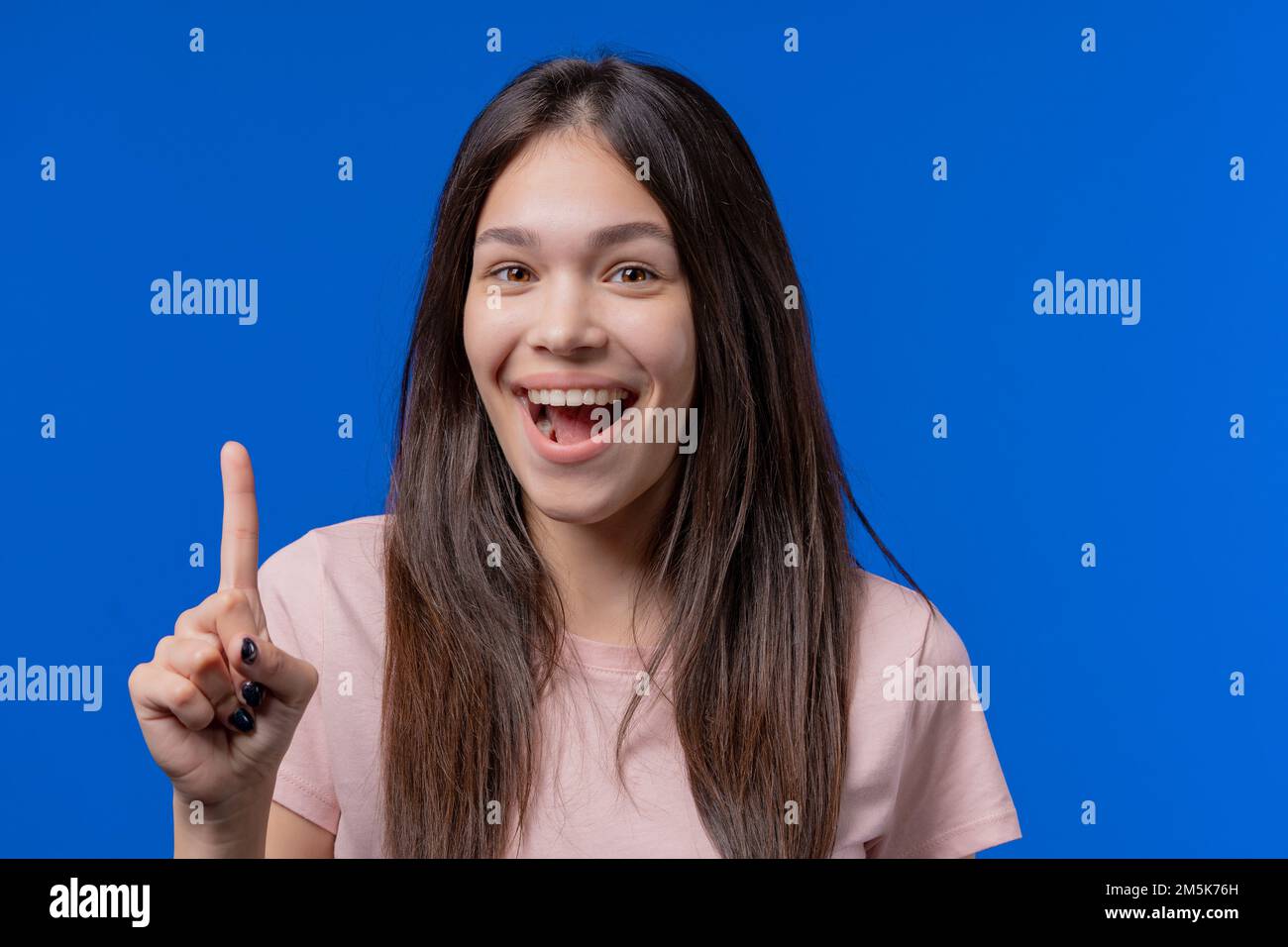 Happy teen girl having idea eureka moment, pointing finger up on blue ...