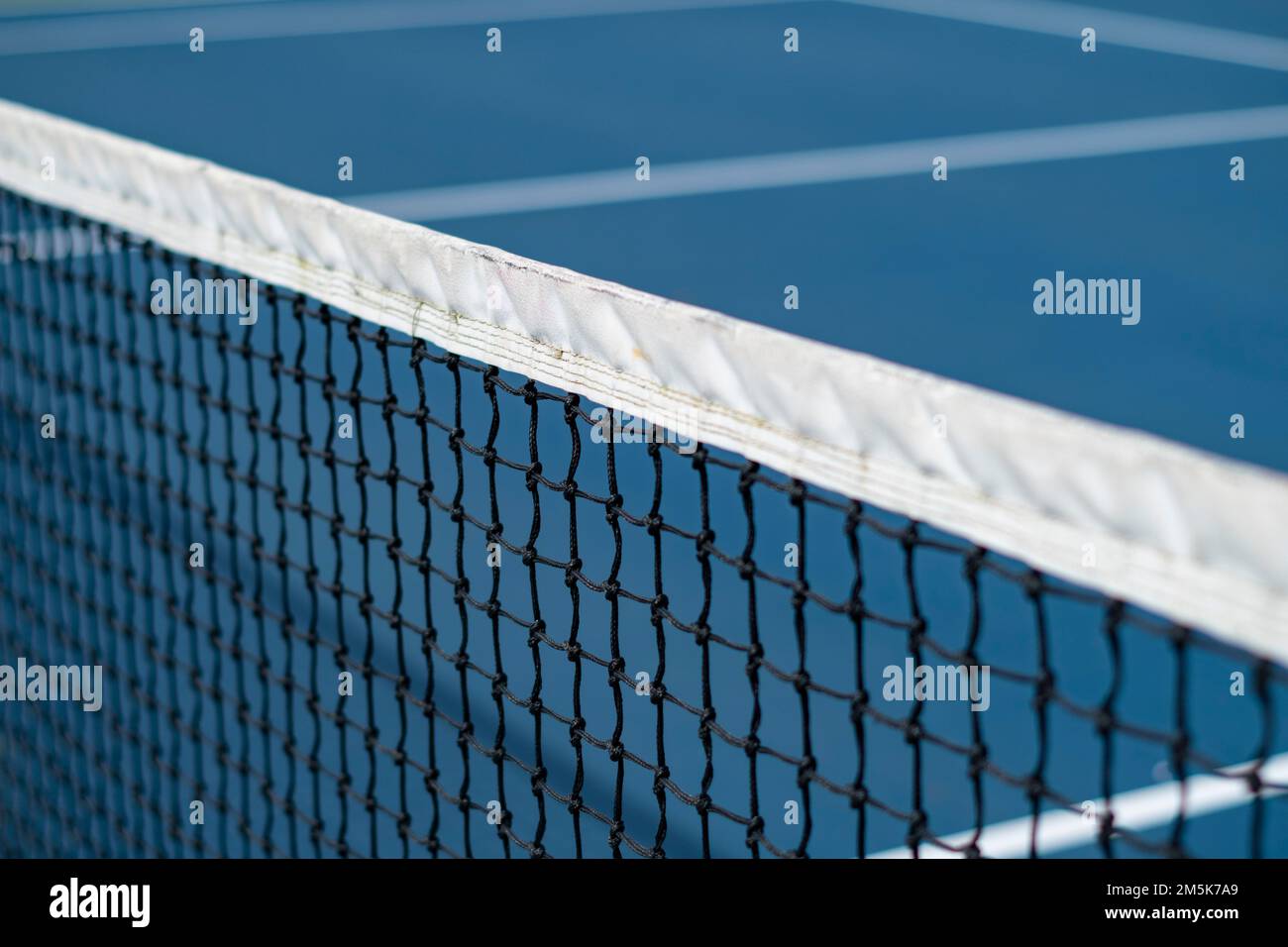 A close-up of the diagonal tennis net with white lines on a blue court ...