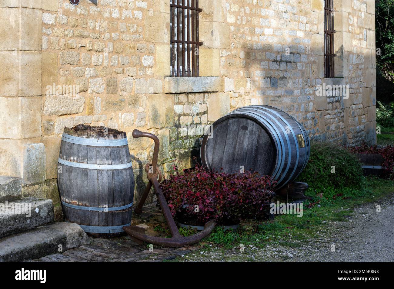 Two wooden barrels and an anchor outside in front of a stone wall and ...