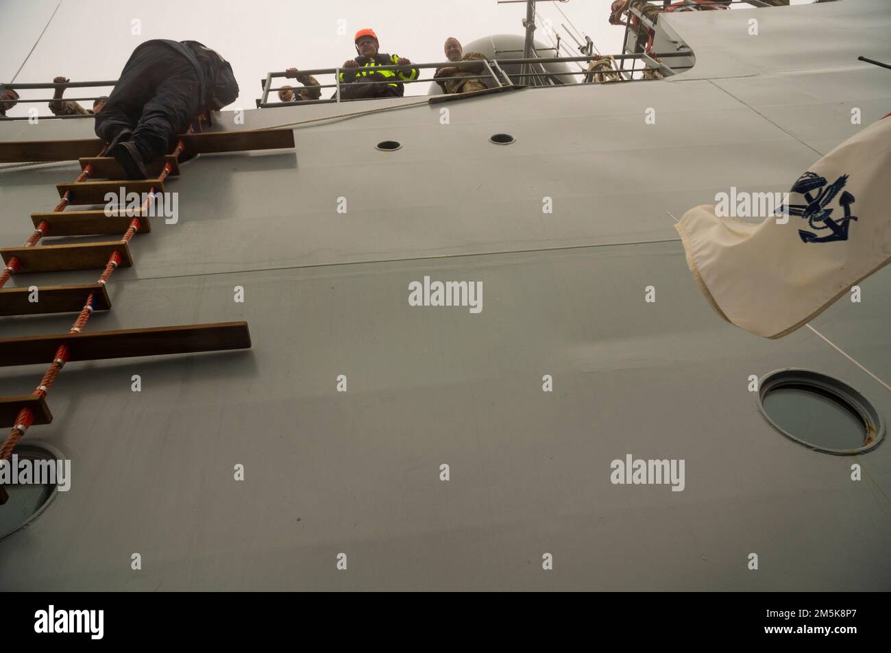 Sailor climbs up ladder from small boat alongside the Royal Danish Navy ...
