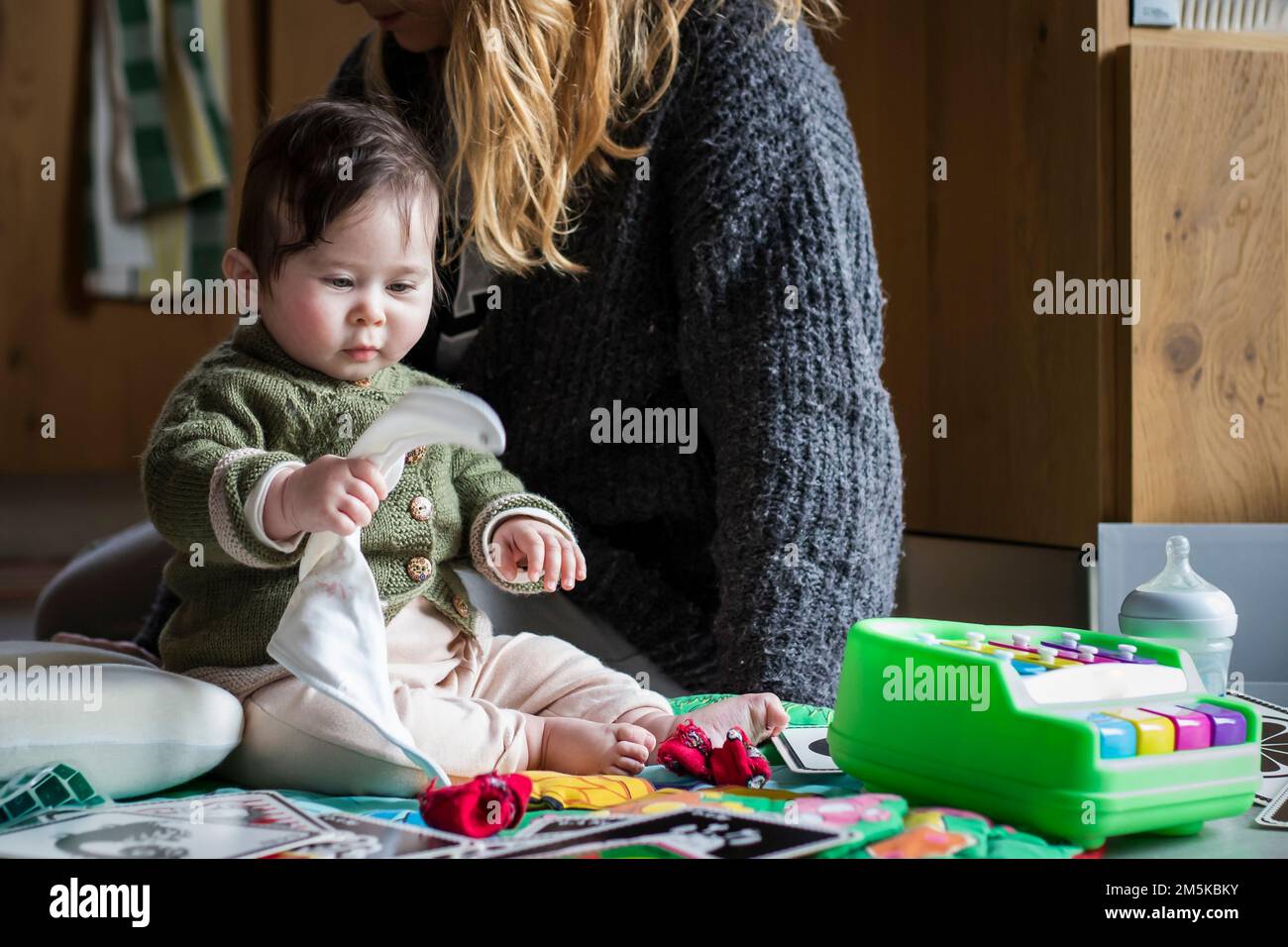 adorable baby playing on a play rug, next to her mother. Real home ...