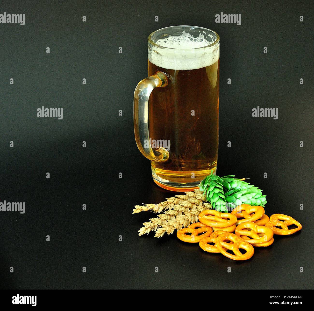 A glass mug with light beer and foam on a black background, next to it ...