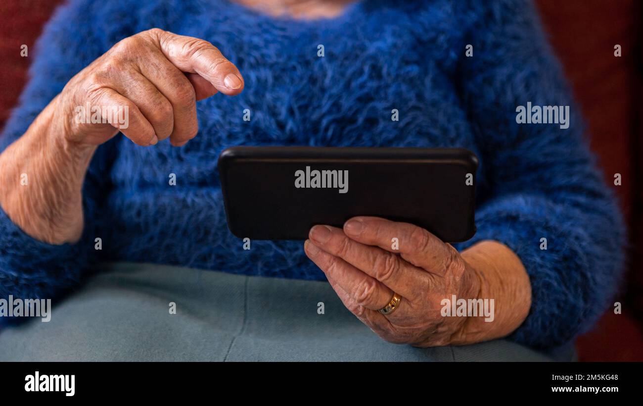 Old woman at home using a mobile phone. Wrinkled hands of grandmother ...