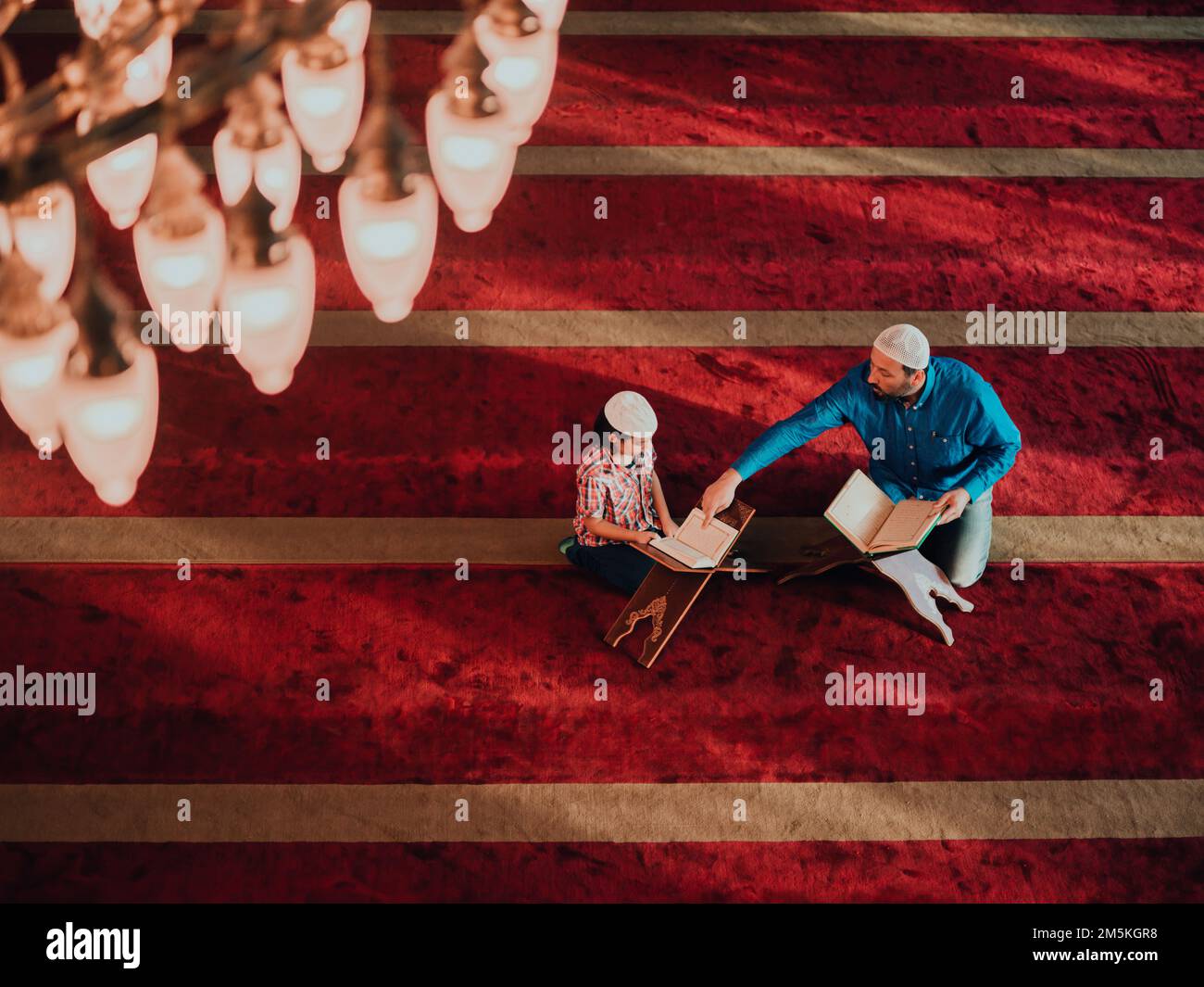 Muslim prayer father and son in mosque praying and reading holly book Quran together islamic ...