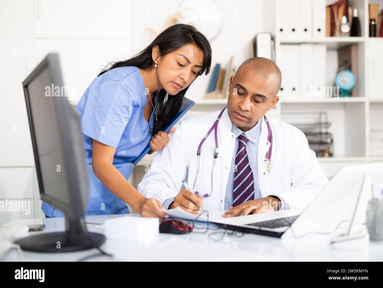 Doctor signing papers brought by female assisant in medical office ...