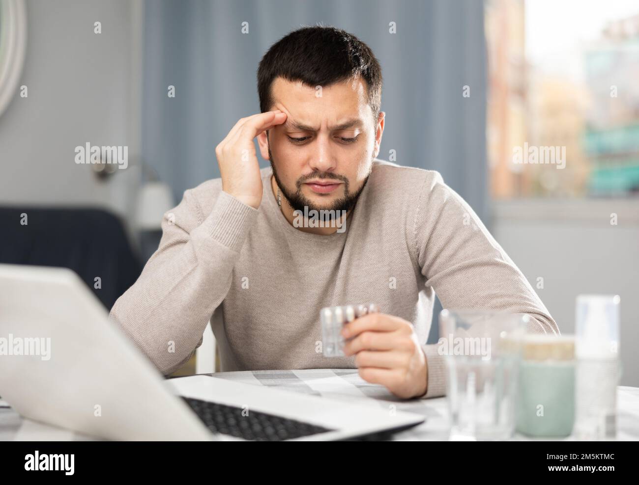 Young man having headache while sitting at home table with laptop Stock ...