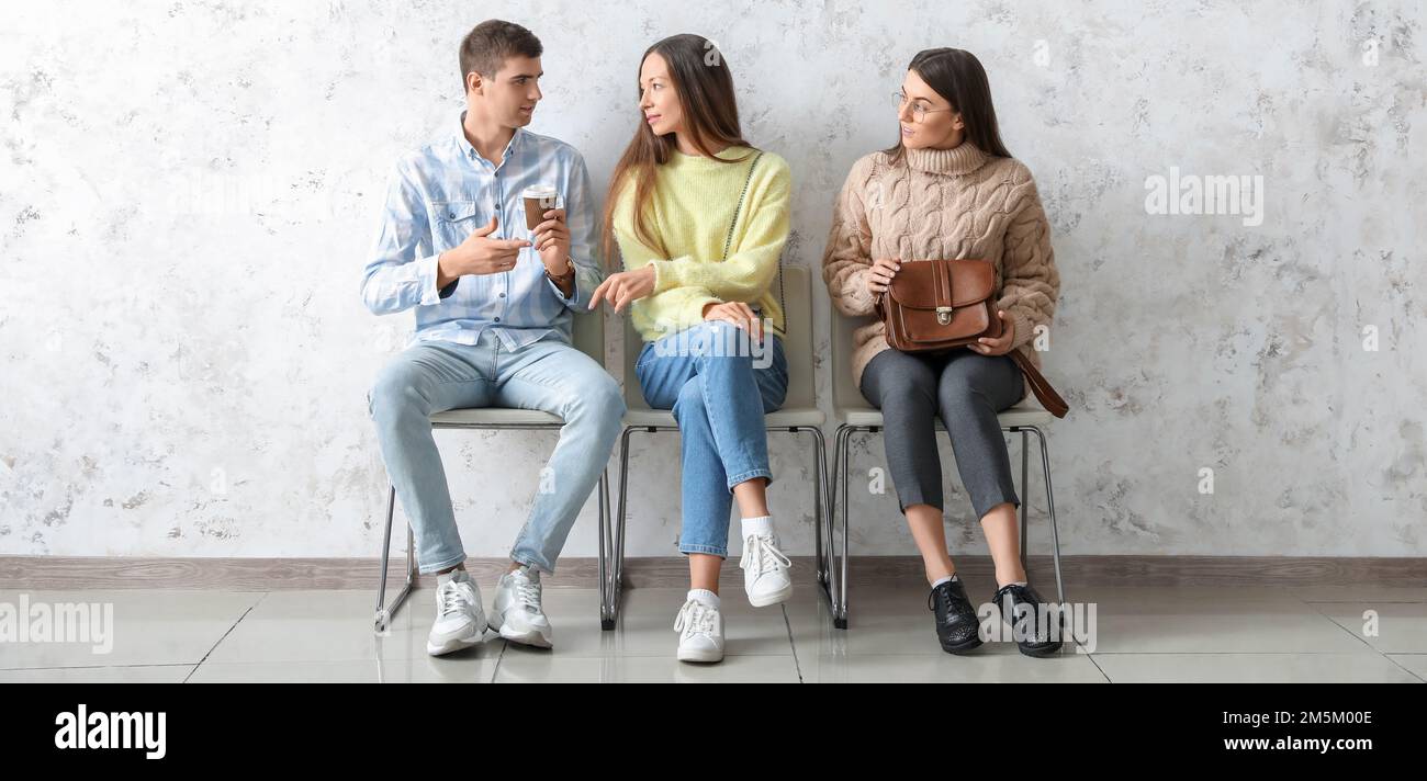 People waiting in line while sitting near light wall Stock Photo - Alamy