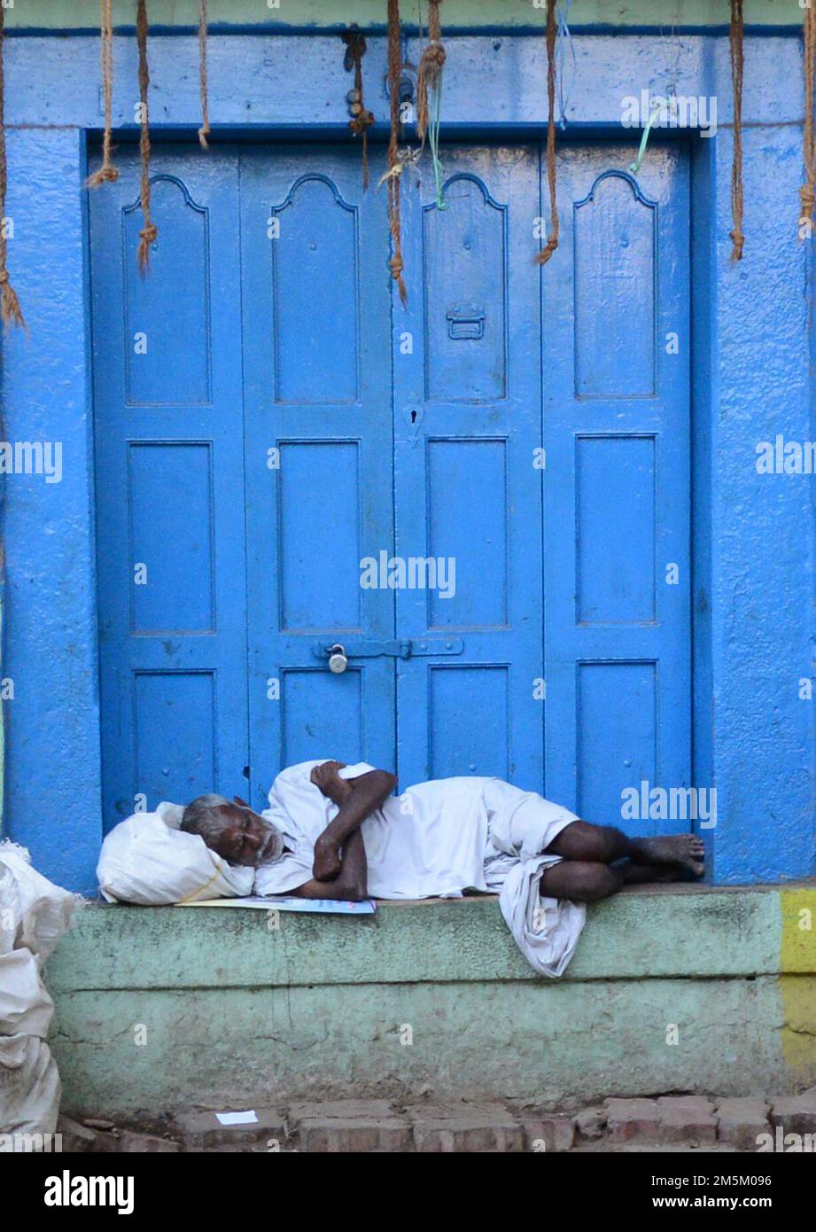 A Tamil man taking a nap by a blue door in central Madurai, Tamil Nadu ...