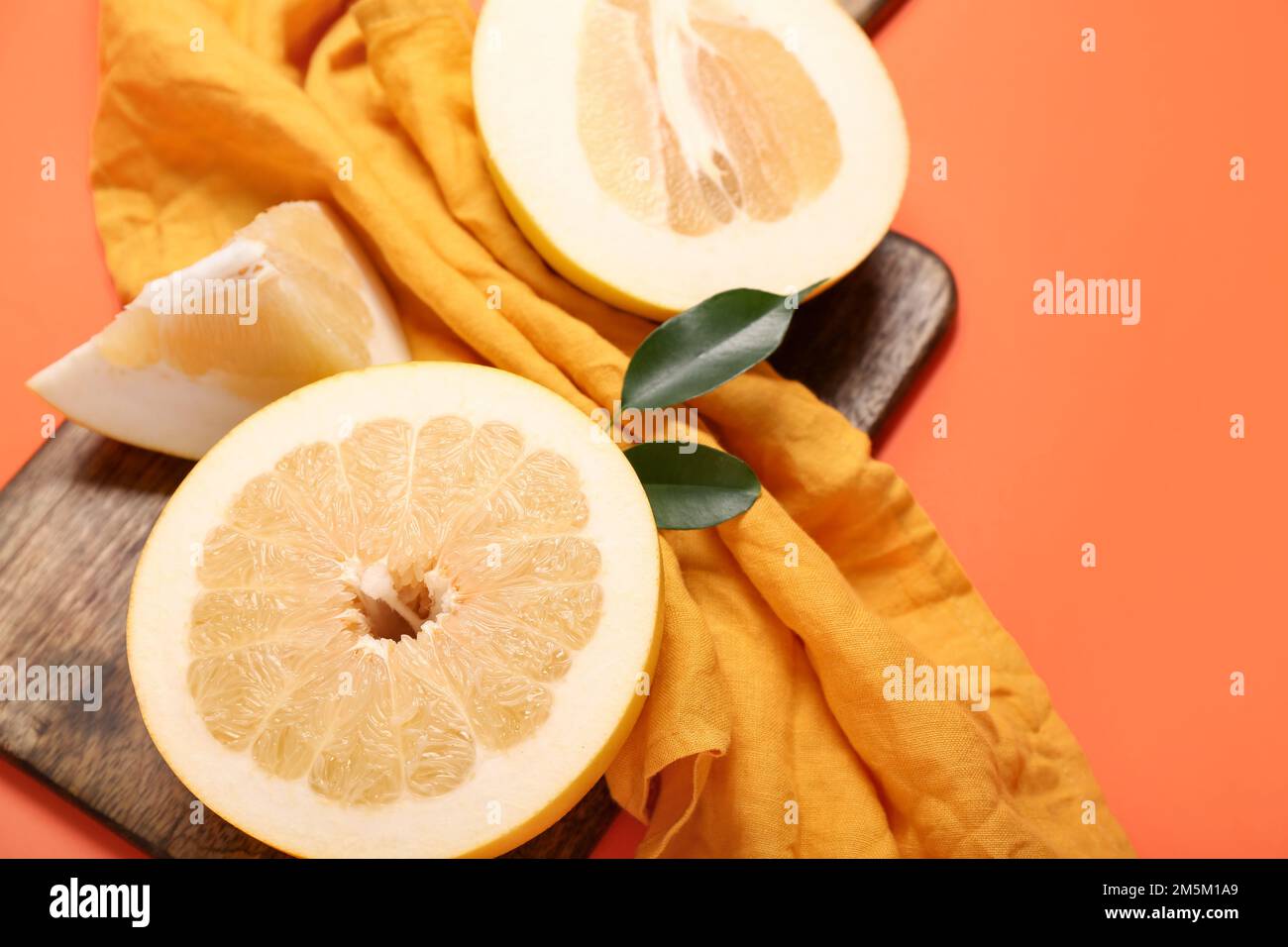 Cutting board with pomelo halves and kitchen towel on orange background ...