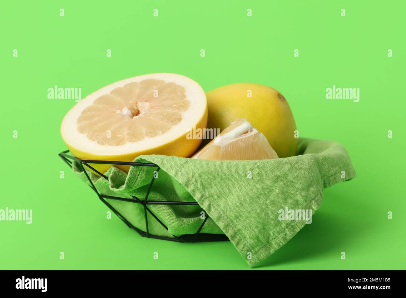 Metal basket of whole and cut sweet ripe pomelo fruits on green ...