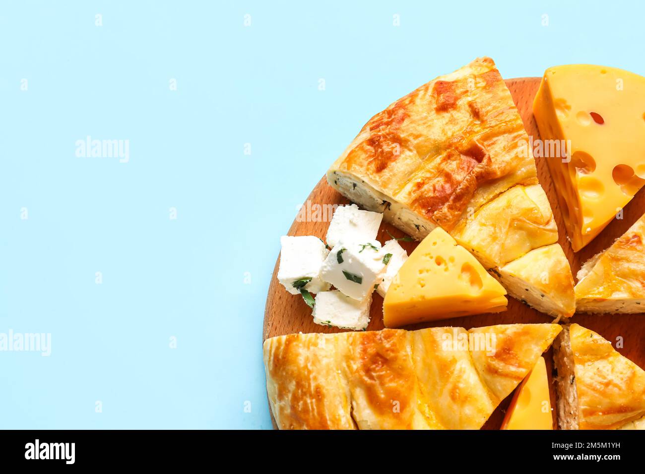 Board with pieces of delicious cheese pie and ingredients on blue ...
