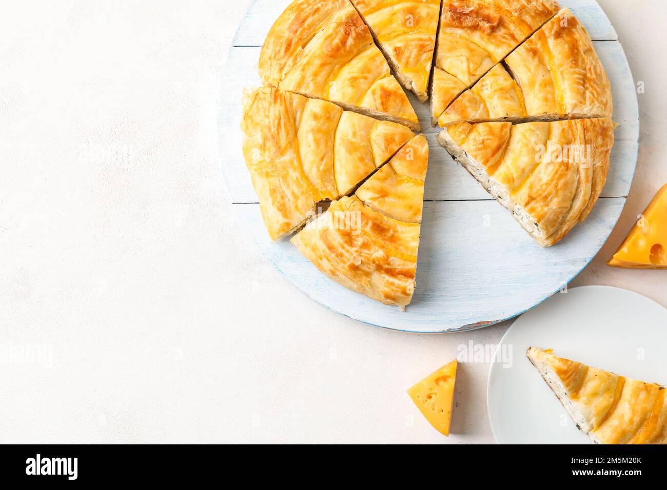 Board and plate with pieces of delicious cheese pie on white table ...